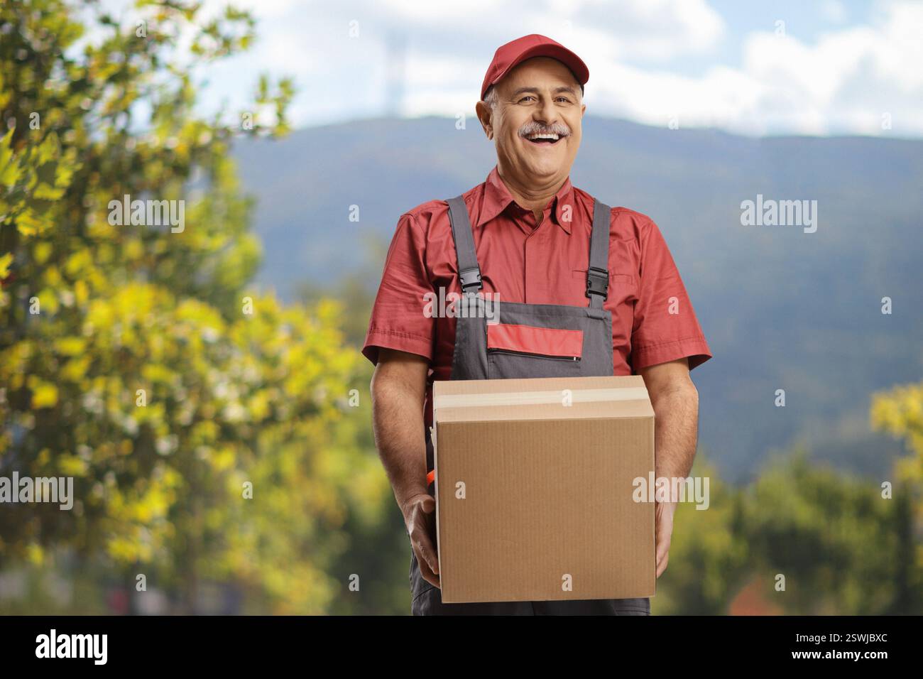Mature delivery man carrying a cardboard box outdoors Stock Photo - Alamy