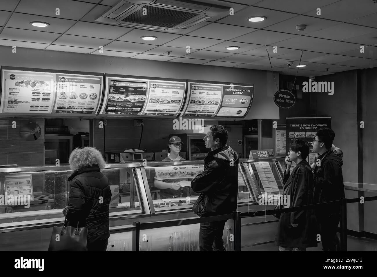 People wait in line inside a modern fast-food restaurant under bright ...