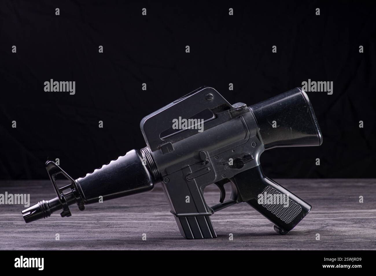 A dark metallic toy gun placed on a wooden surface against a black ...