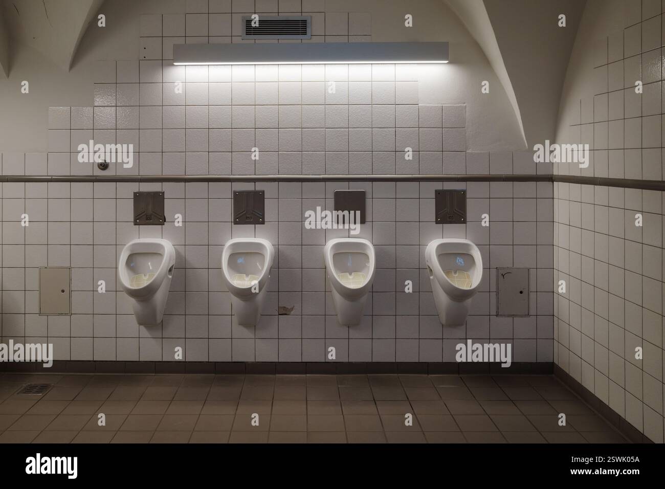 A clean yet slightly aged public restroom featuring four white ceramic ...