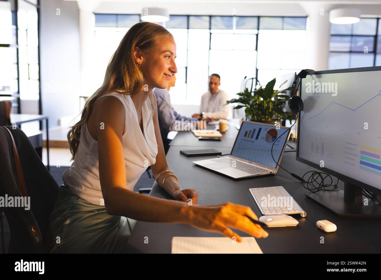 Analyzing data on computer, businesswoman in modern office, smiling confidently. technology ...