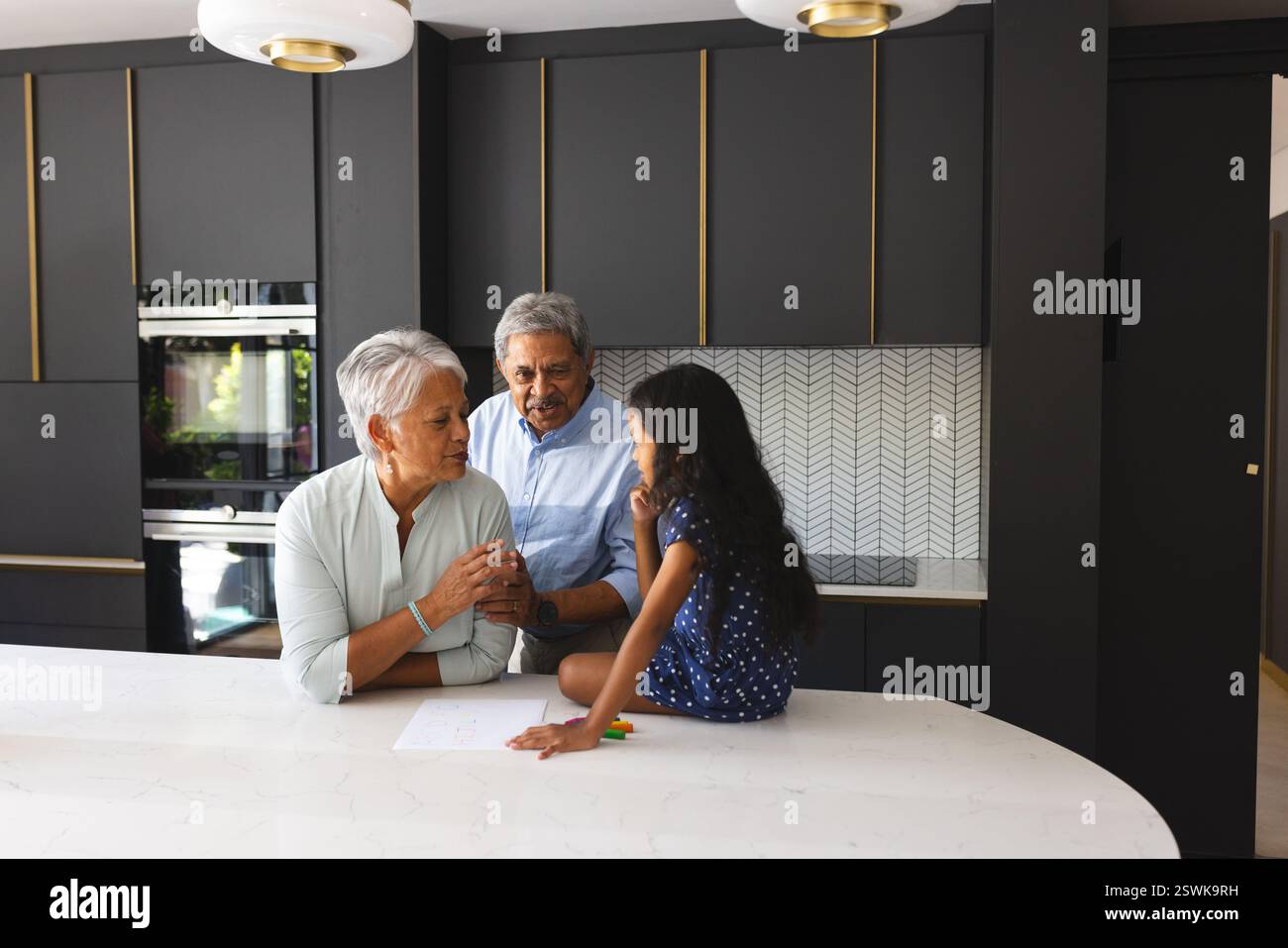 Granddaughter drawing with grandparents at kitchen counter, sharing ...