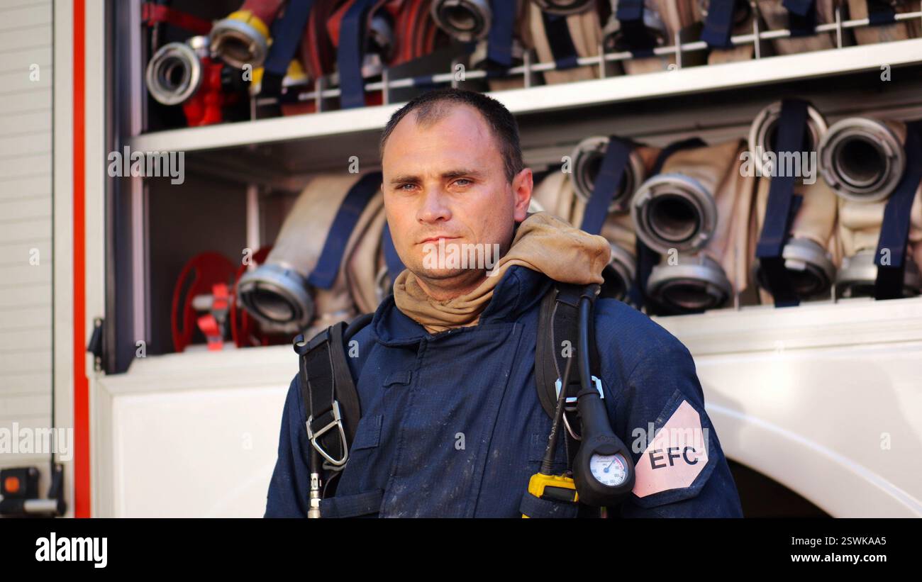 Portrait of confident male firefighter standing near a fire engine ...