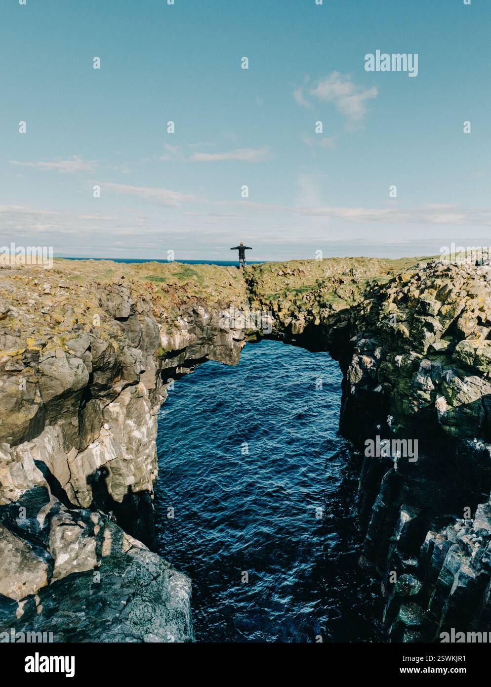 Adventurer standing on a natural rock arch over the ocean in Arnarstapi ...