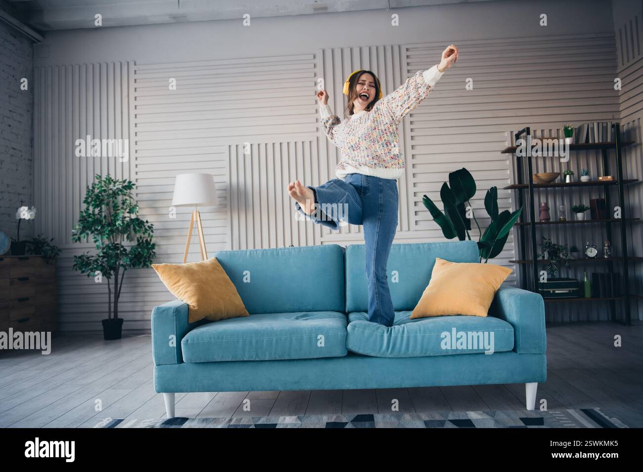 Energetic young woman dancing joyfully on couch in stylish and cozy ...