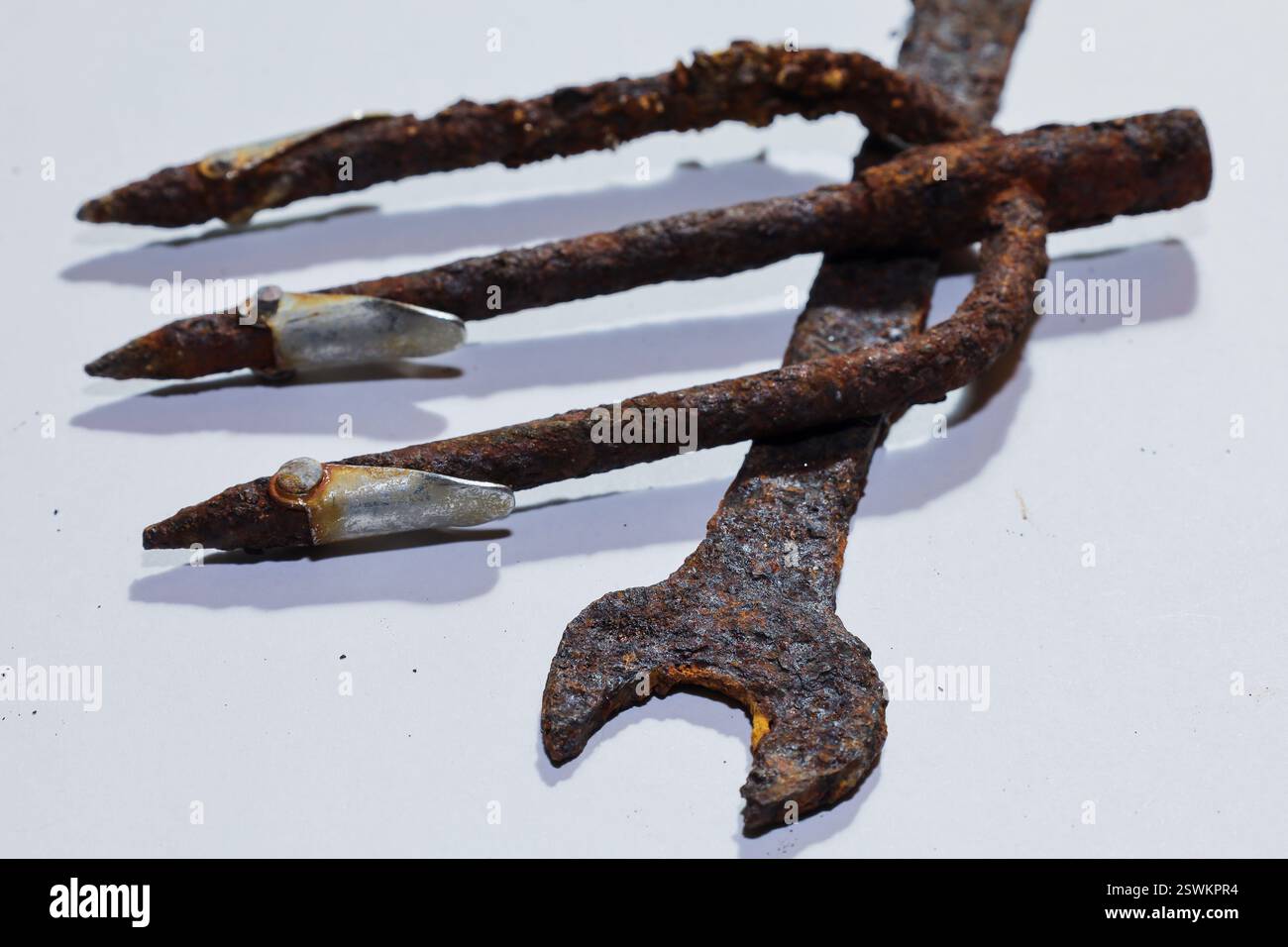 A close-up of a rusty fishing trident resting on a corroded wrench ...