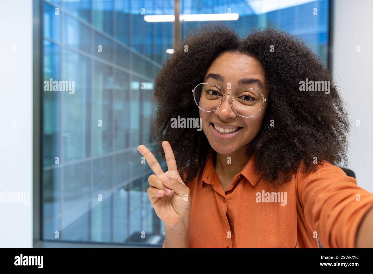A happy young woman with afro hair and round glasses shows the peace ...