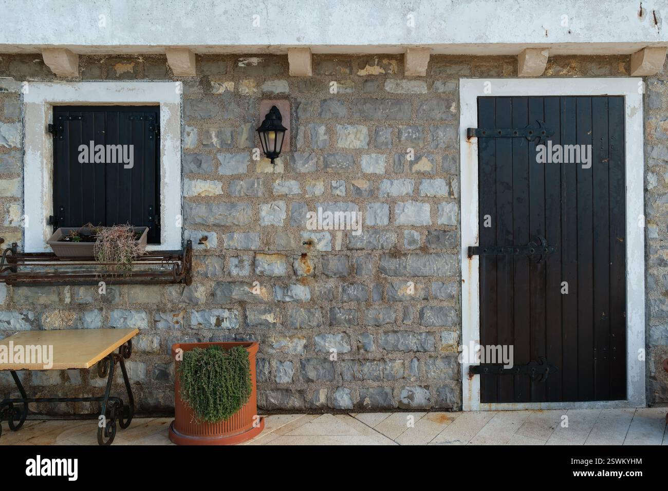 Rustic Mediterranean stone wall with a black wooden door and shuttered ...