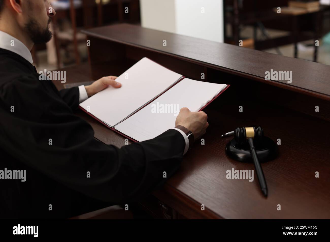 Judge with folder of documents at wooden table in courtroom, closeup ...