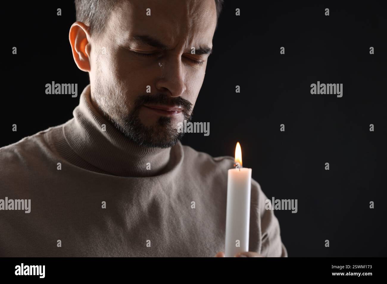 Sad man with burning candle crying on black background, space for text ...