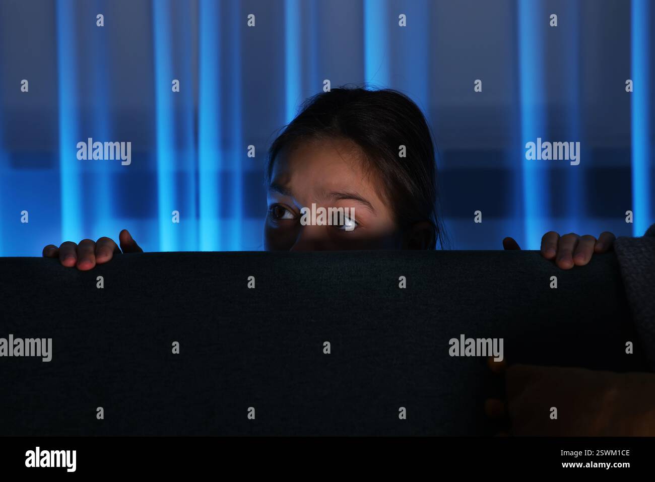 Scared girl hiding behind sofa at night Stock Photo - Alamy