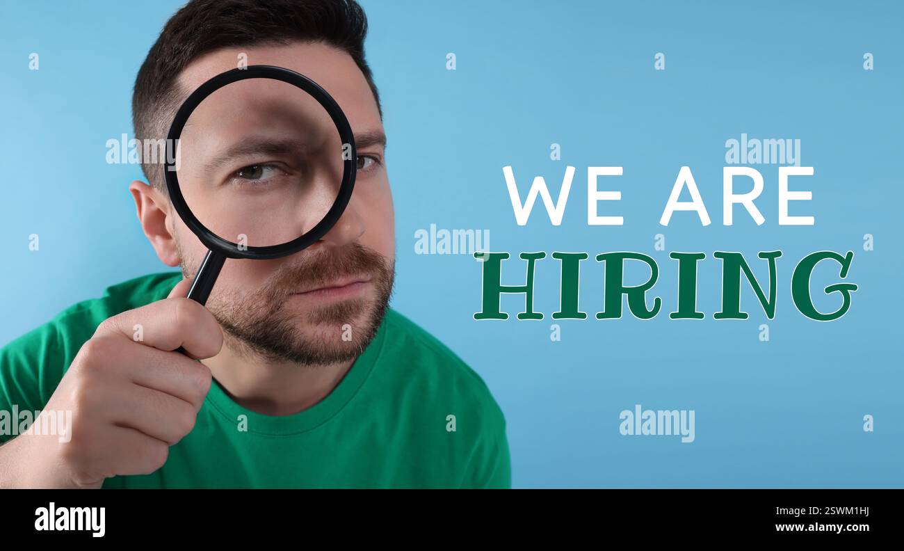 We are hiring. Man looking through magnifying glass on light blue ...