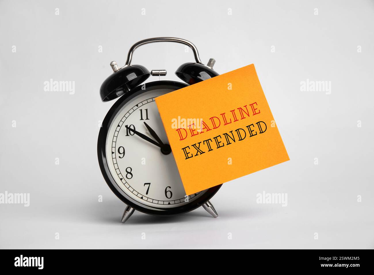 Paper note with text Deadline Extended attached to alarm clock on white ...