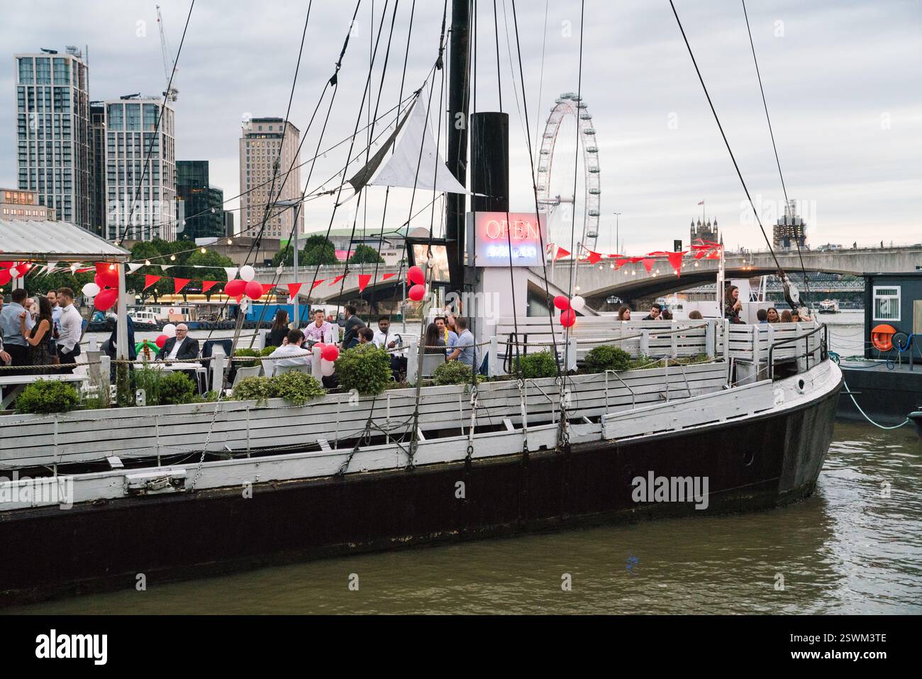 Londoners enjoy drinks on a floating bar, moored near the London Eye ...