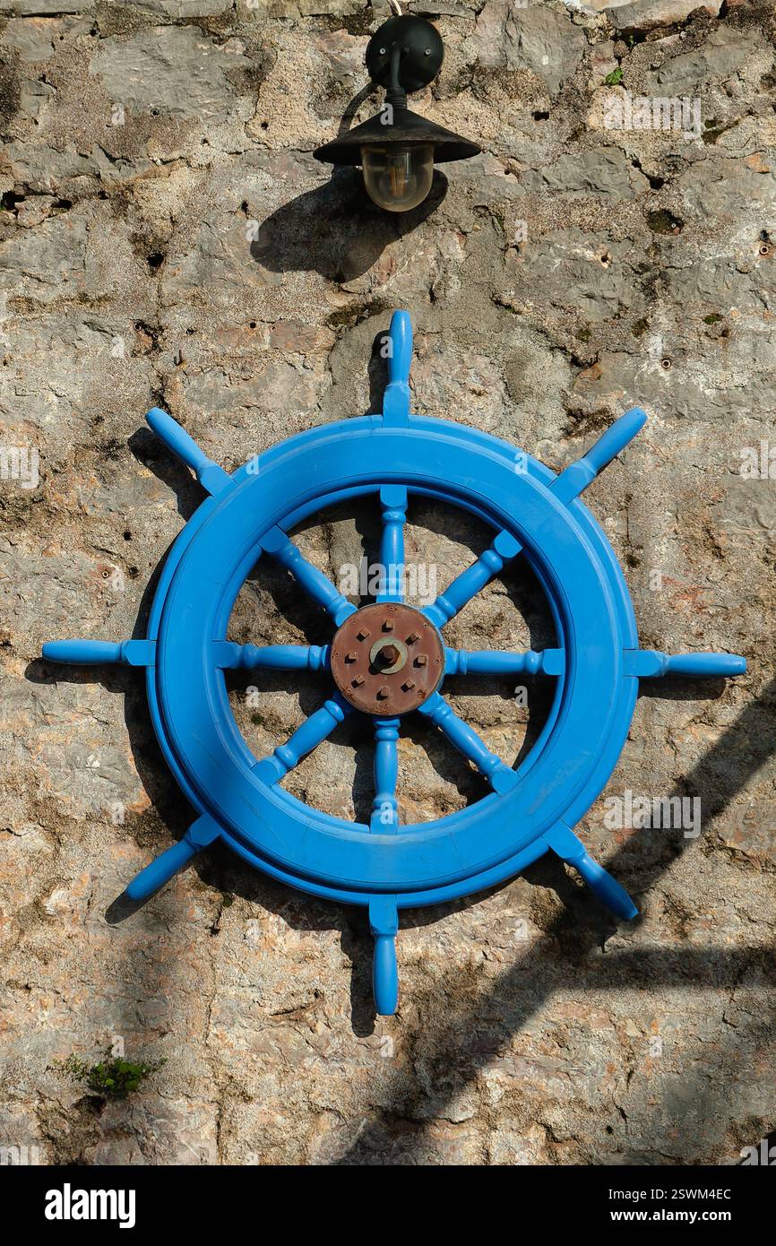 Wooden blue ship wheel from a fishing boat mounted on a stone wall ...