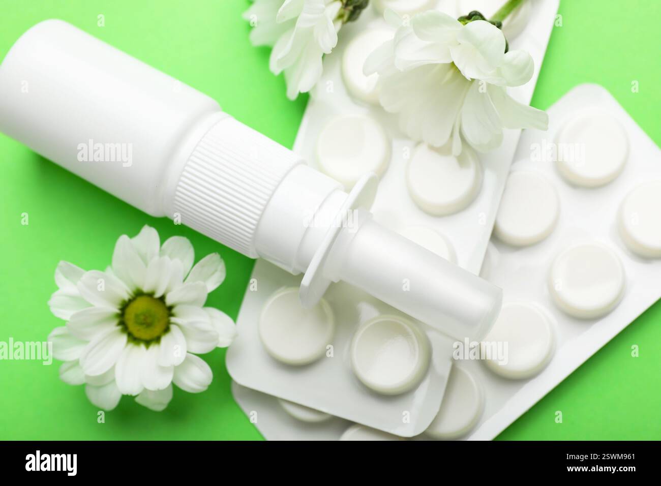 Allergy treatment. Nasal spray, pills and flowers on green background ...