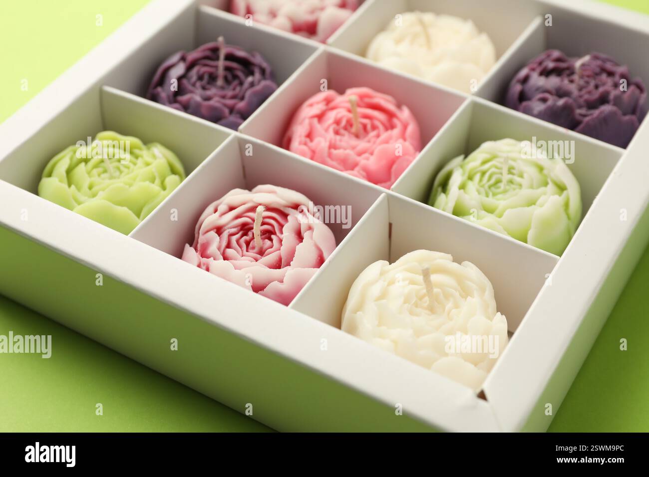 Beautiful flower-shaped candles in box on light green background ...