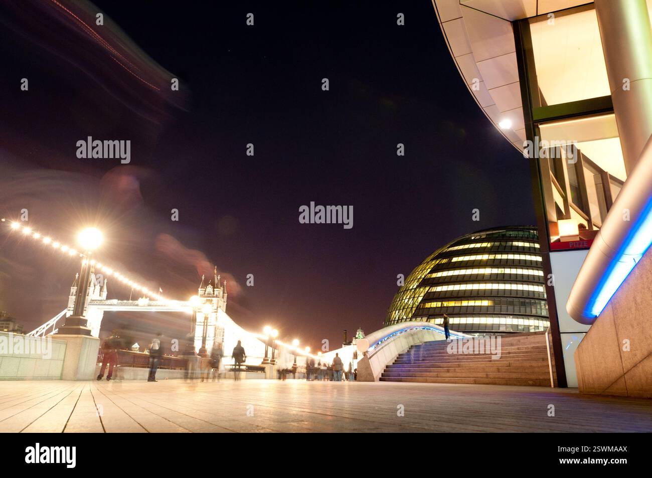 Pedestrians walk across Tower Bridge, London, at night, past the City ...