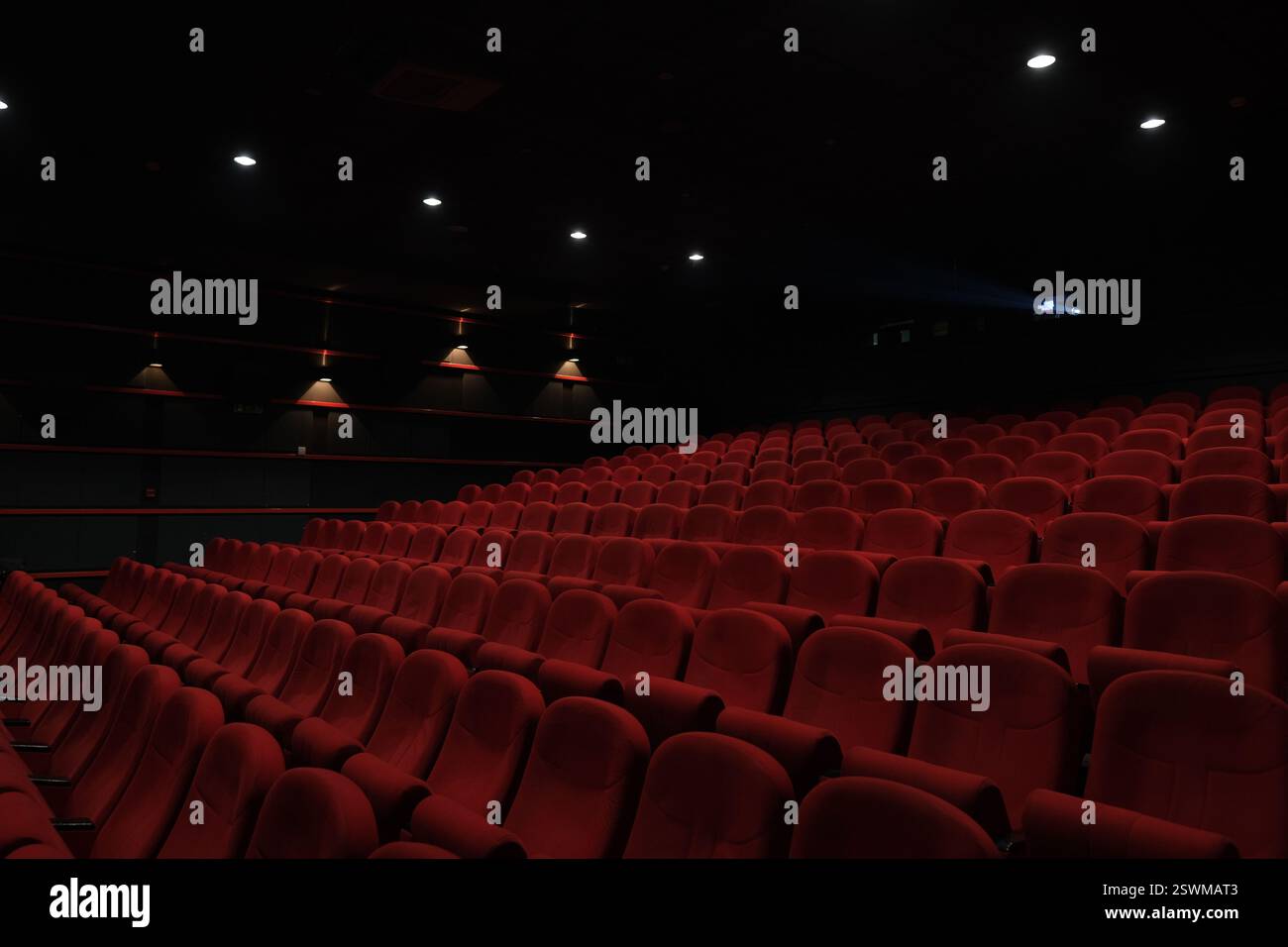 Rows of empty red seats fill a darkened movie theater illuminated only ...