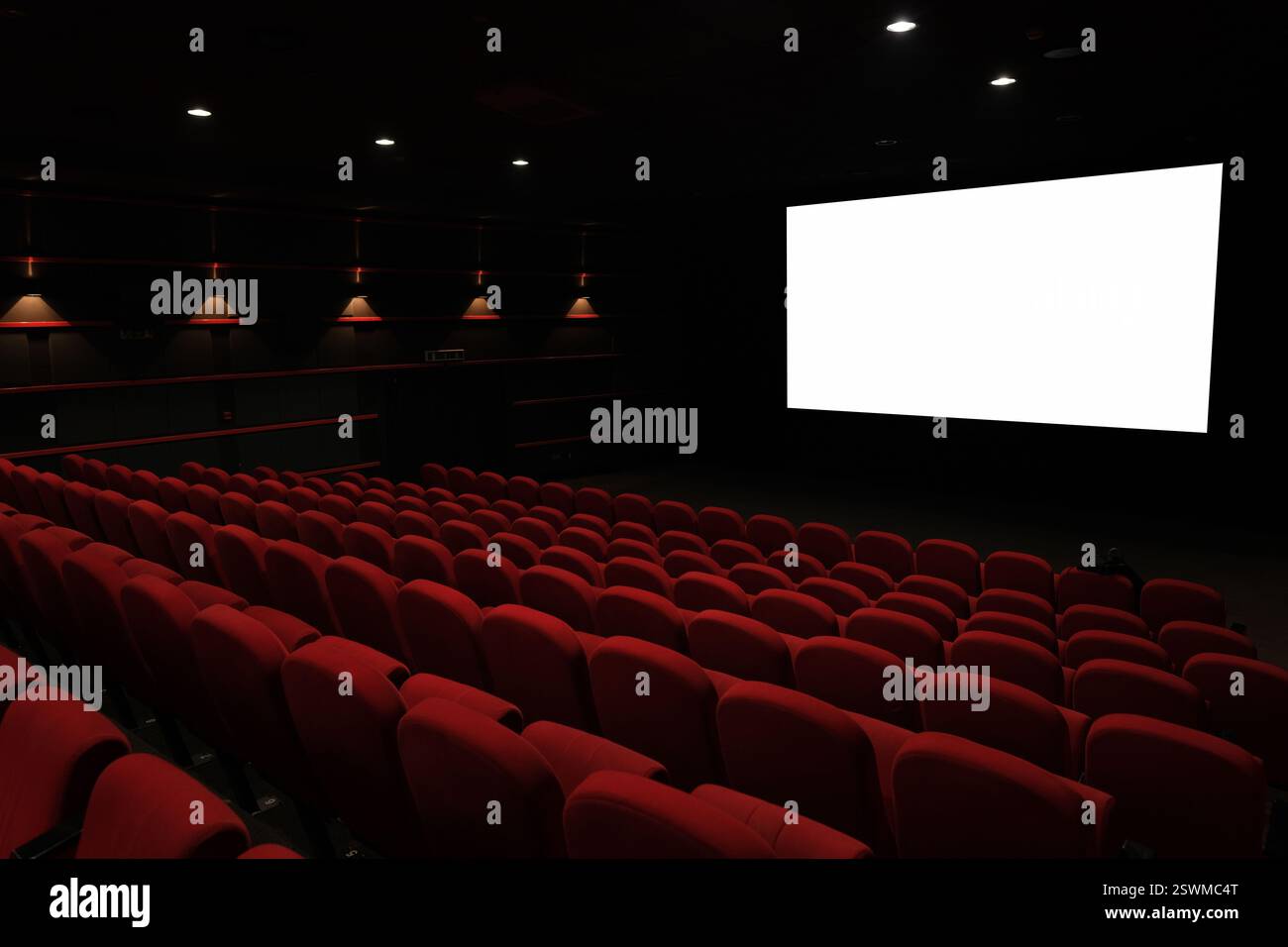 Empty cinema interior with rows of red seats facing a large white screen ready for a movie ...