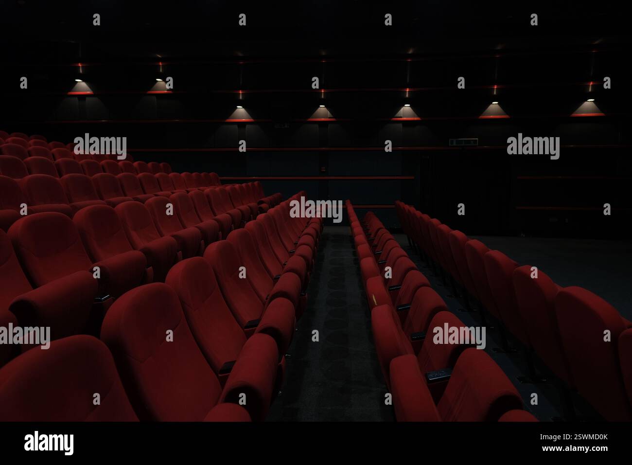 Rows of empty red seats in dark theater lit by dim lights overhead creating a sense of ...