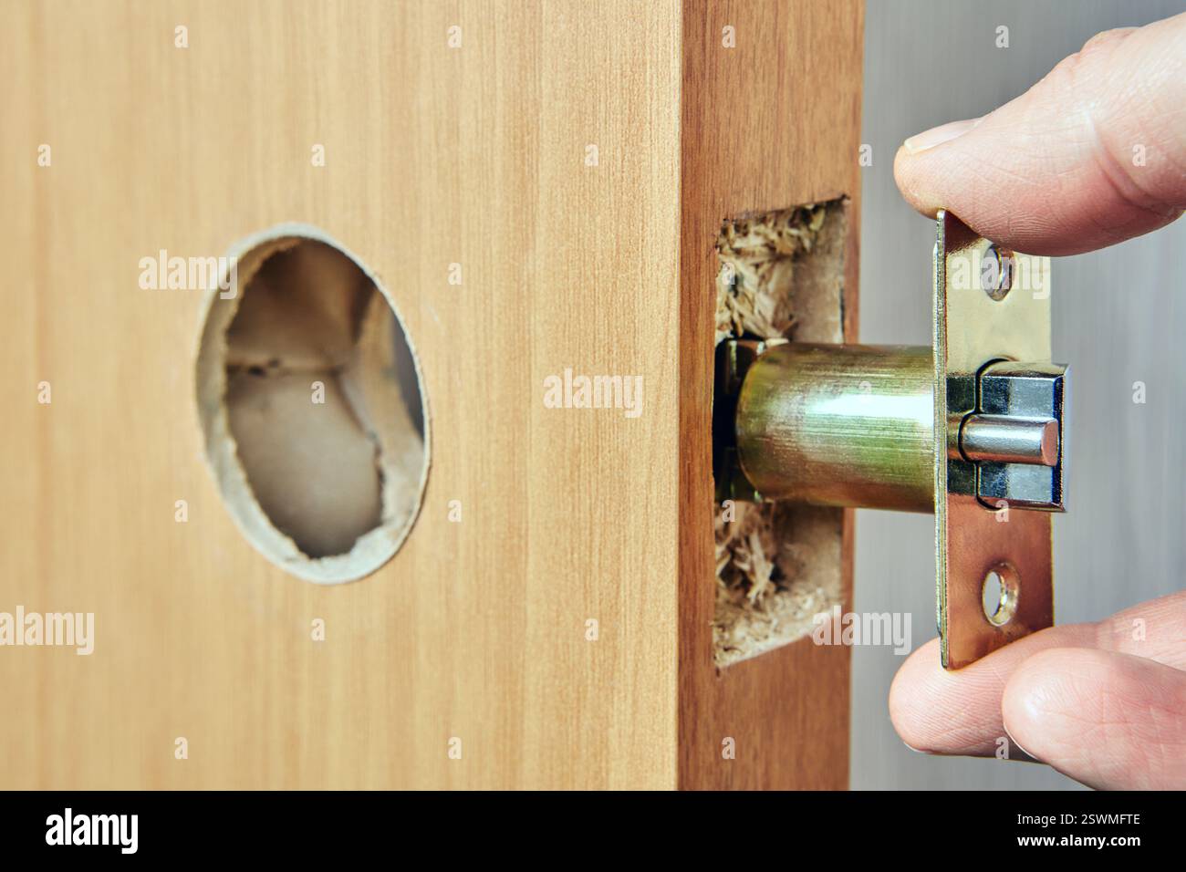 Brass latch mechanism is being installed into wooden door frame, with ...