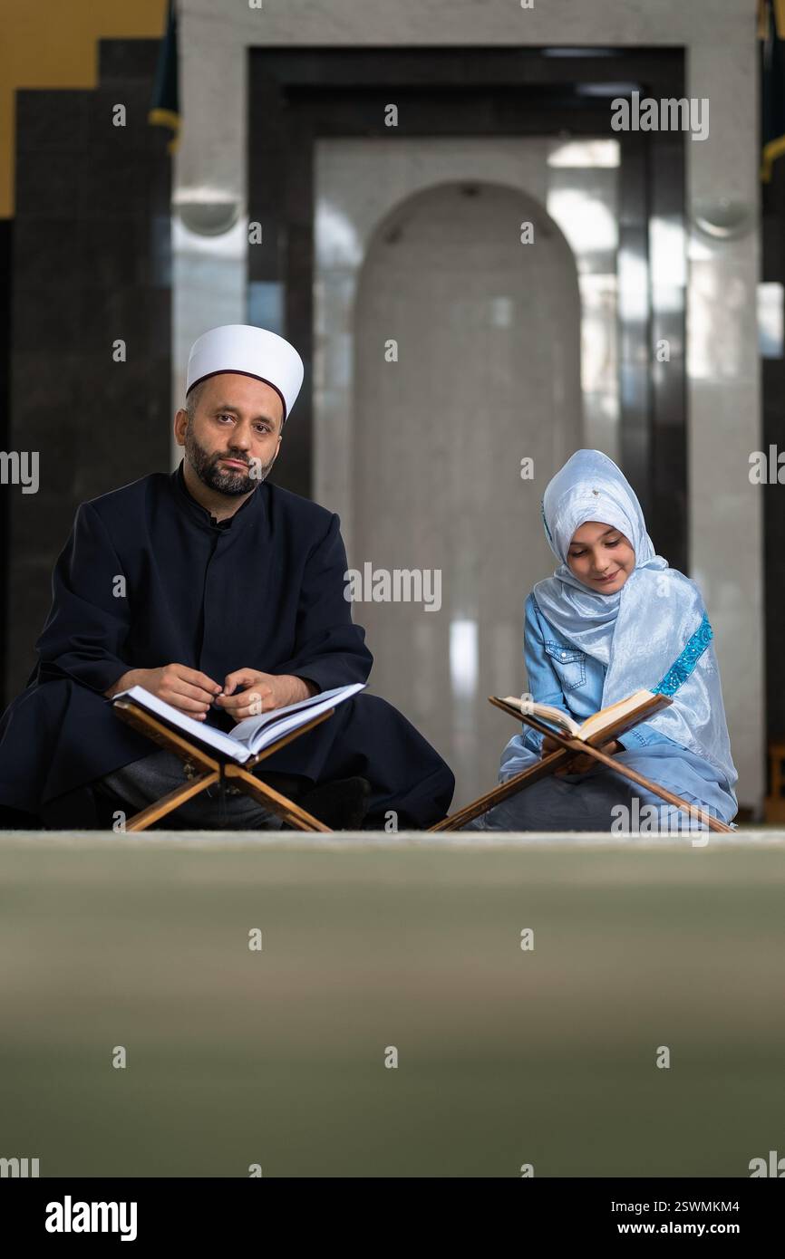 A Muslim teacher teaches child girl to read a holy book Quran inside ...