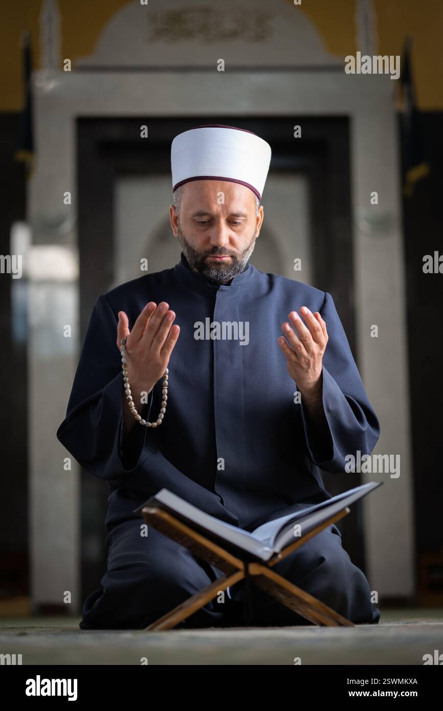 A Muslim prayer man praying with hands up while reading a Quran inside ...
