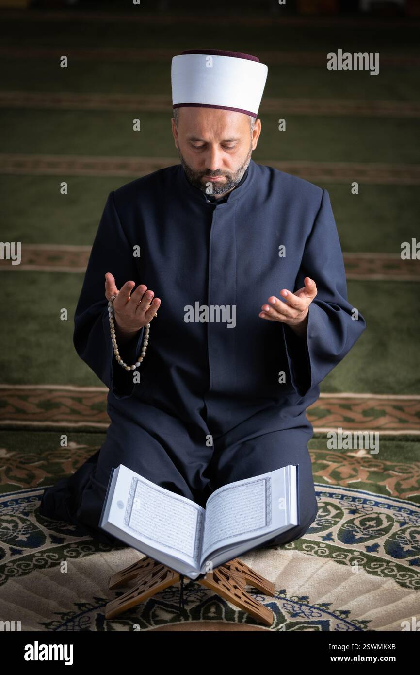 A Muslim prayer man praying with hands up while reading a Quran inside ...