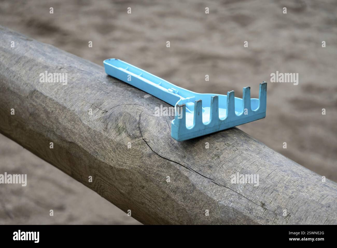 Small blue plastic toy rake left on wooden beam in children's ...