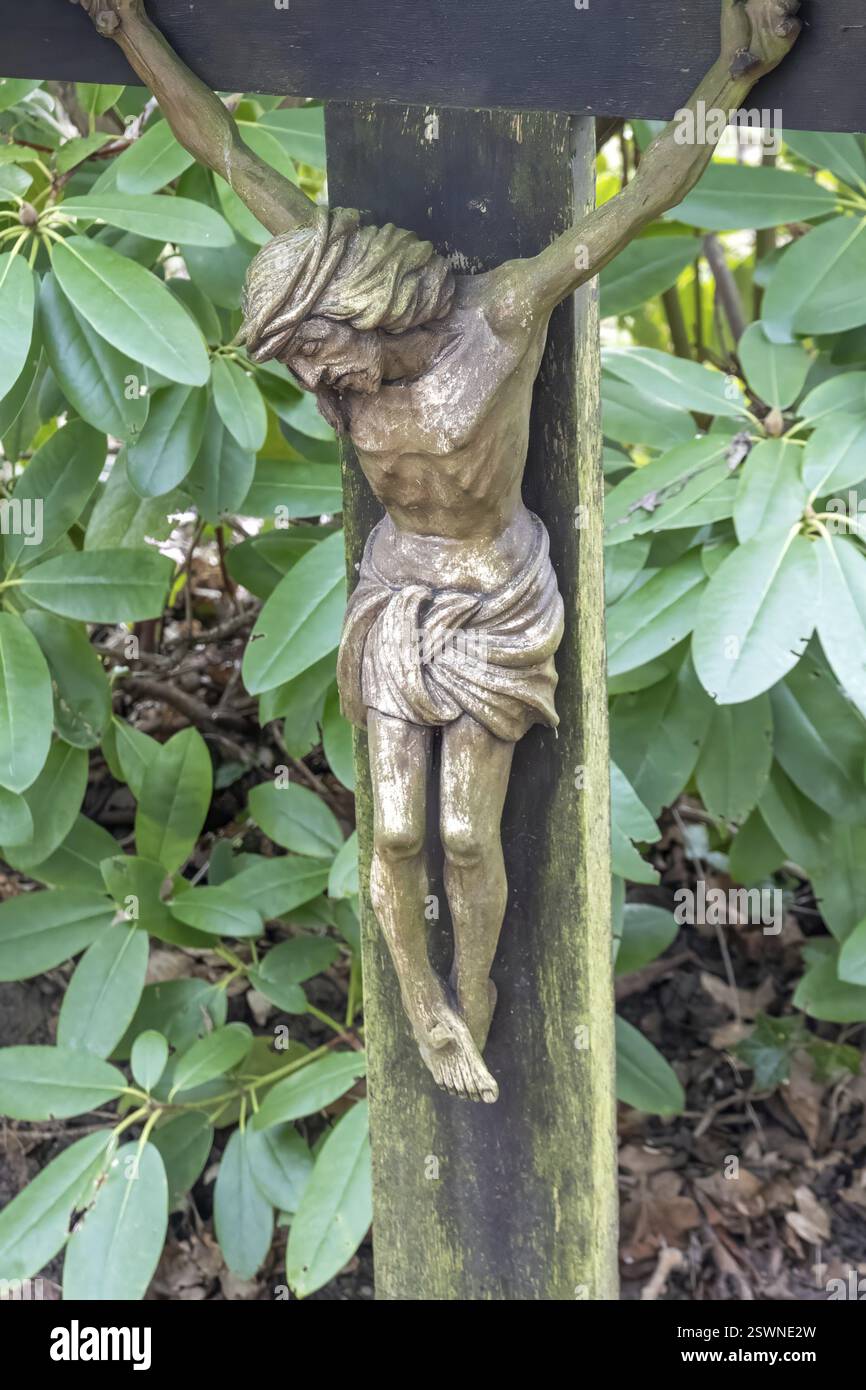 Wooden statue of jesus christ hanging on a cross, surrounded by green ...