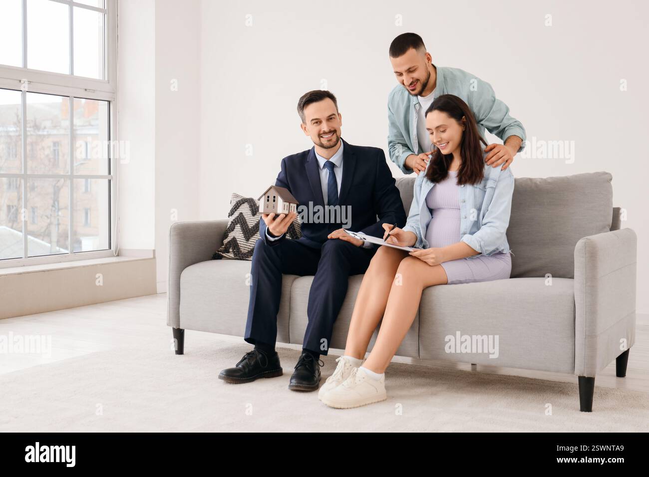 Male realtor with pregnant couple filling out house rental agreement on ...