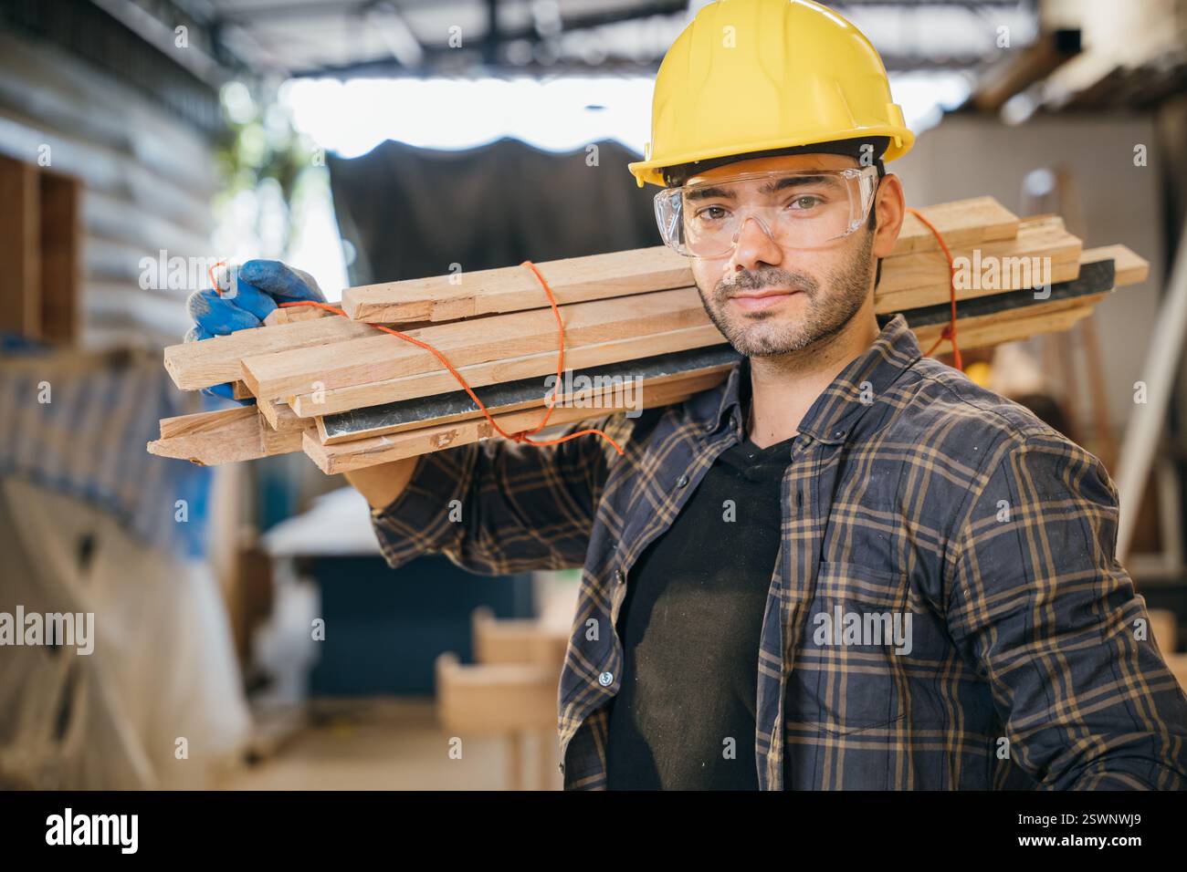 Smiling construction worker in a yellow hardhat and plaid shirt holding ...