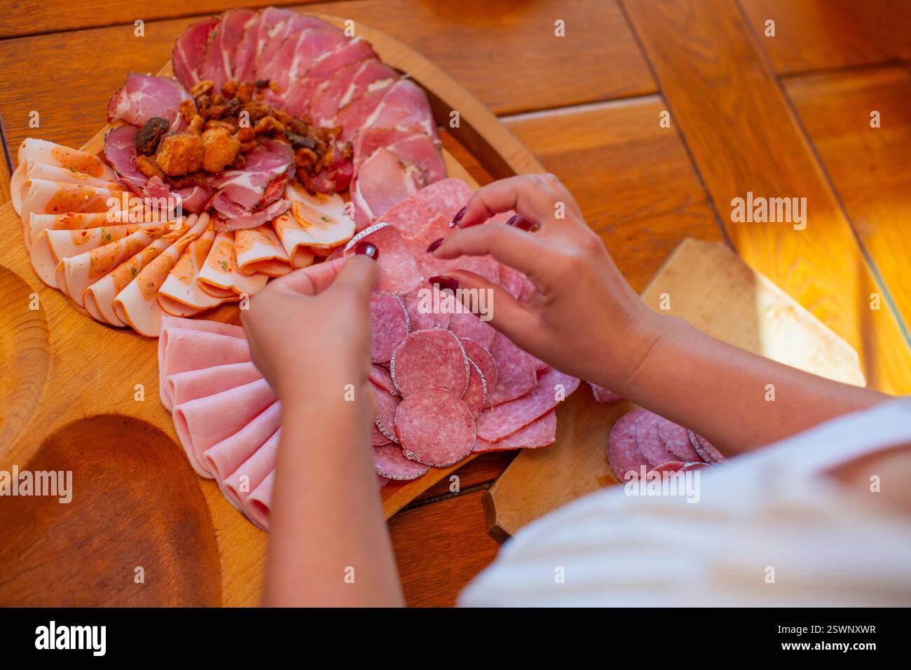 Hands arrange meat slices on a wooden charcuterie board during food ...