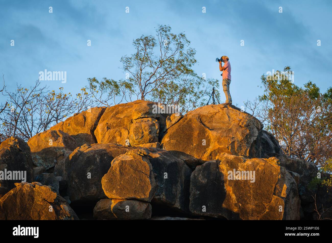 An silhouetted, landscape photographer composes his shot atop a boulder ...