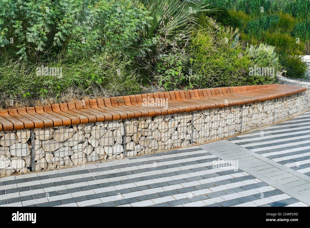 Wooden curved bench from gabion baskets with stones in recreation area ...