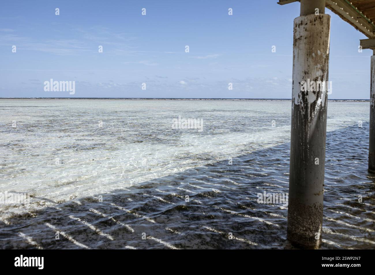 Pillars of a jetty casting shadows on a partially exposed coral reef ...