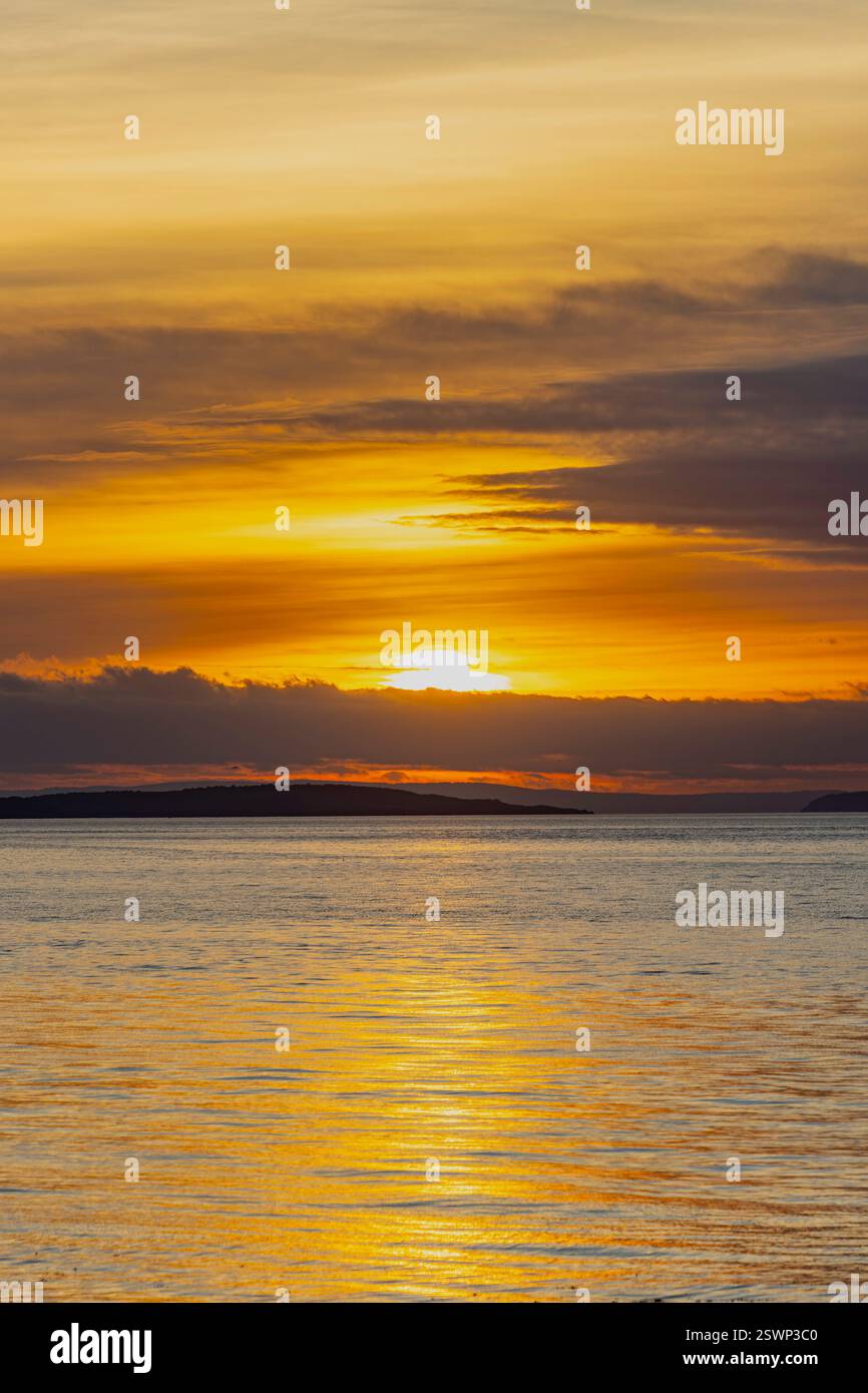 The setting sun disappearing behind some cloud cover with a golden glow ...