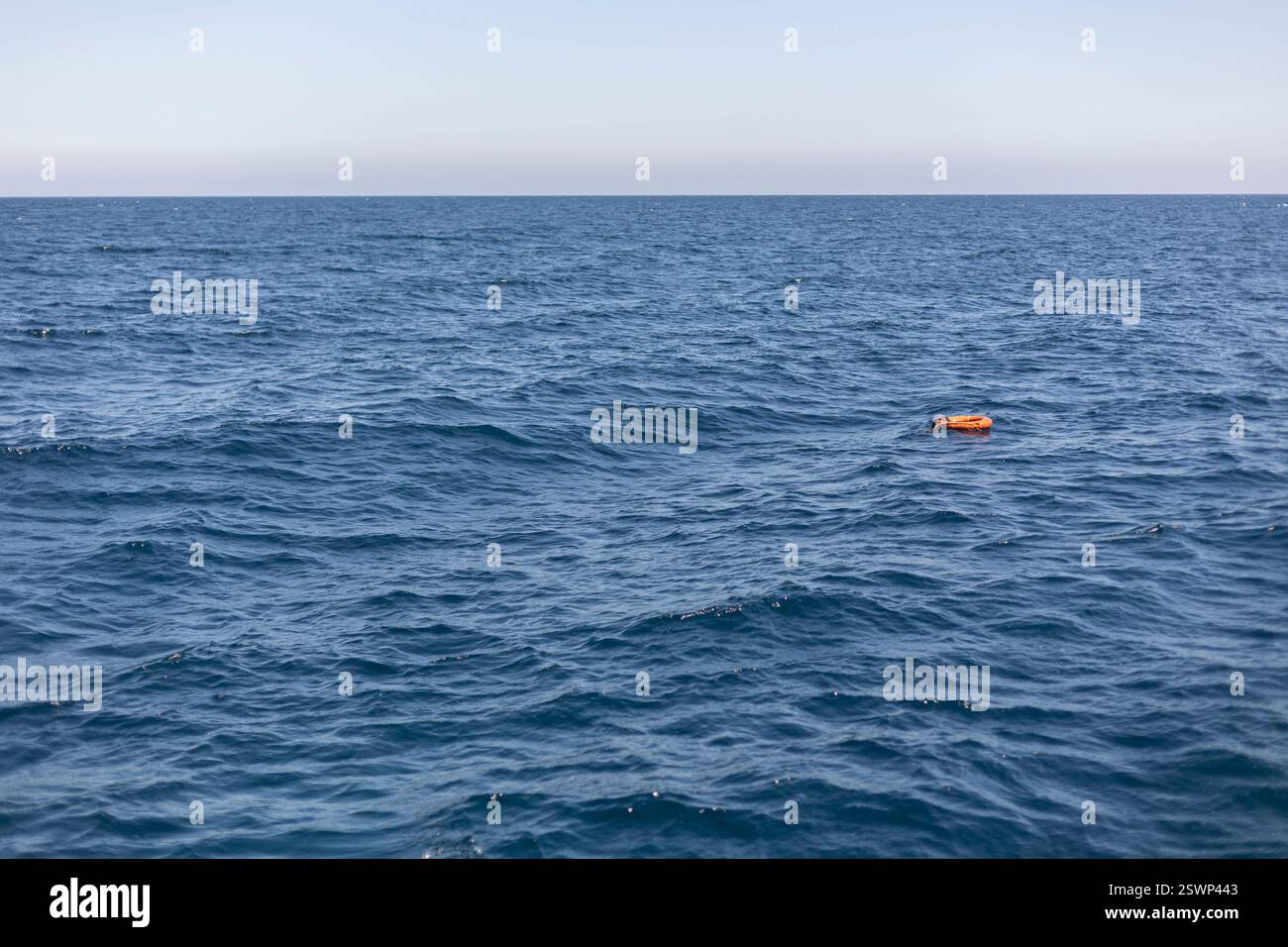 Small orange life raft floating on the surface of a calm blue sea ...