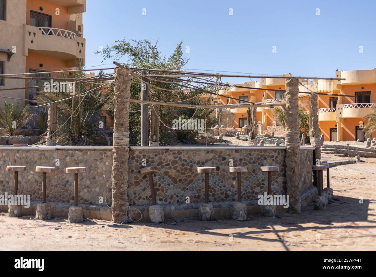 Empty outdoor bar counter featuring a stone wall, wooden stools, and a ...