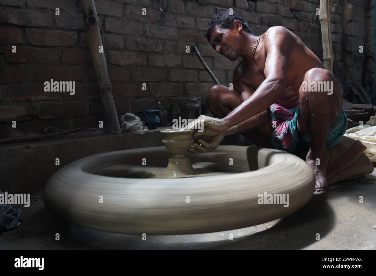 A Bangladeshi potter is making clay pot using pottery wheel in pottery ...