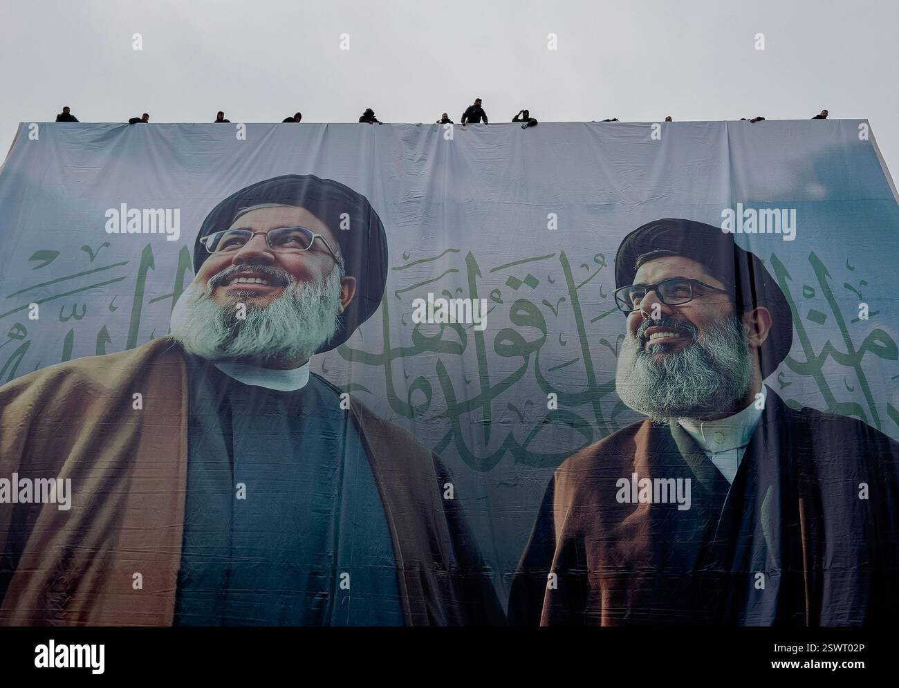 Workers display a giant banner with the portraits of the late Hezbollah ...