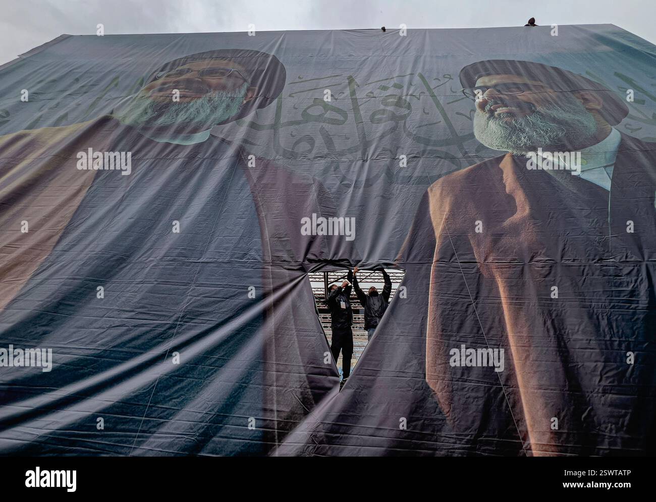 Workers display a giant banner with the portraits of the late Hezbollah ...