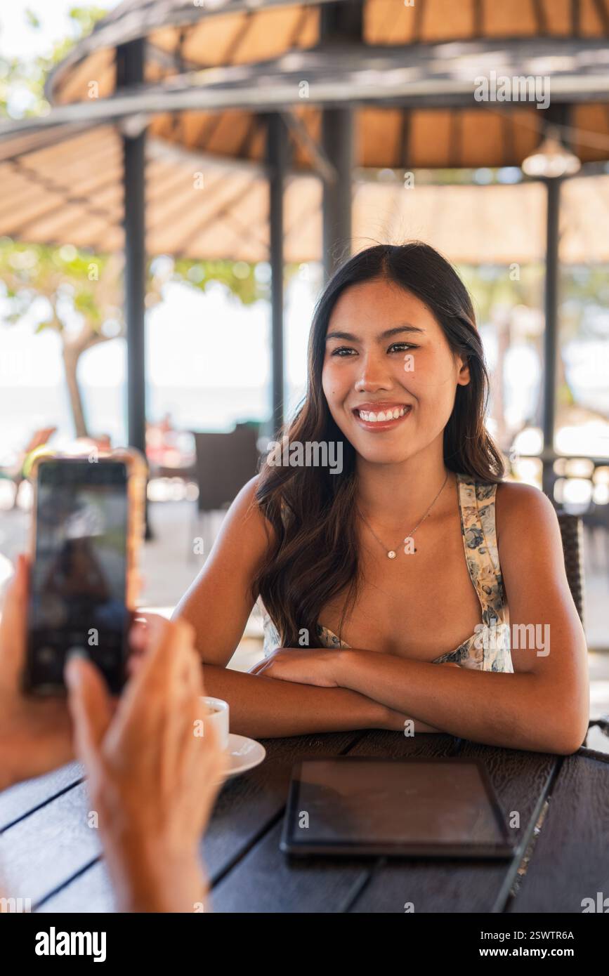 Young Asian woman on the beach smiling while friend taking photo of her ...
