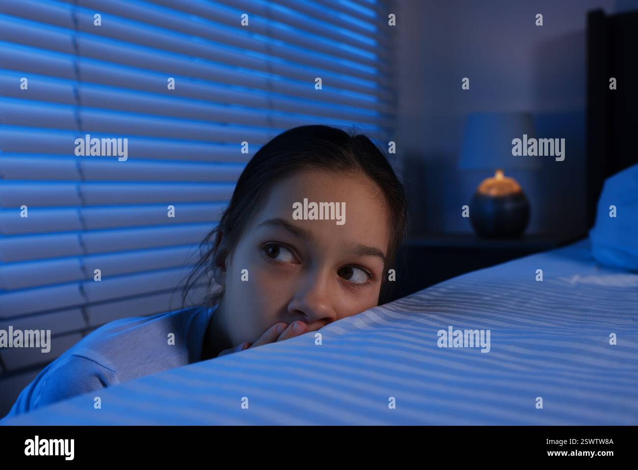 Scared girl hiding behind bed at night Stock Photo - Alamy
