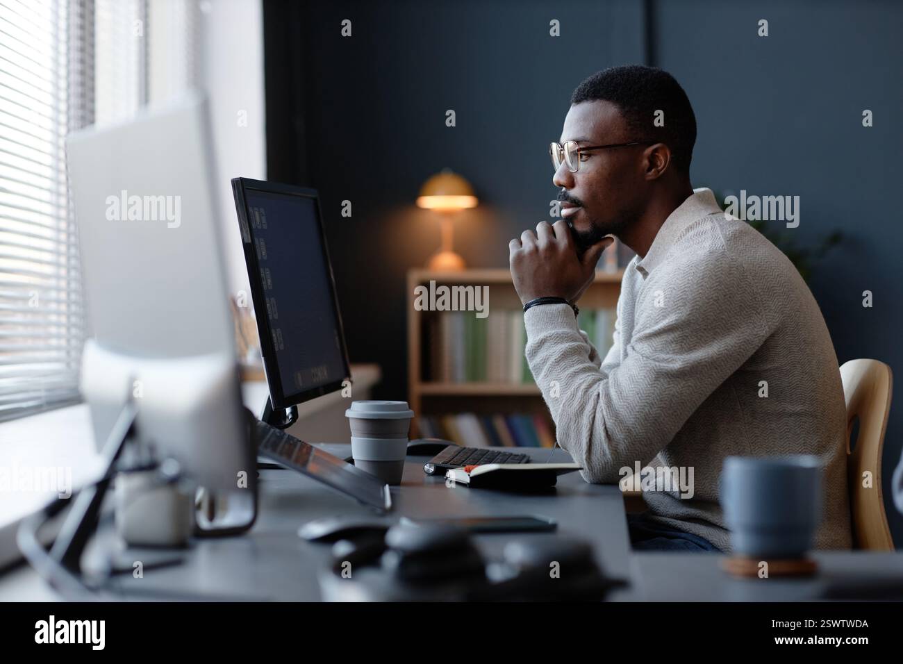 Side view of thoughtful Black office worker with glasses using desktop ...