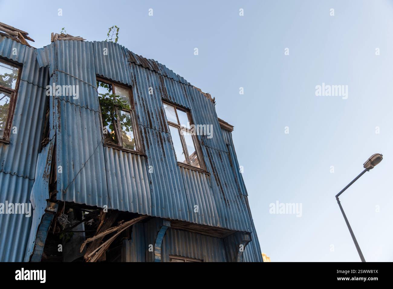 A dilapidated building clad in blue corrugated metal panels, with ...