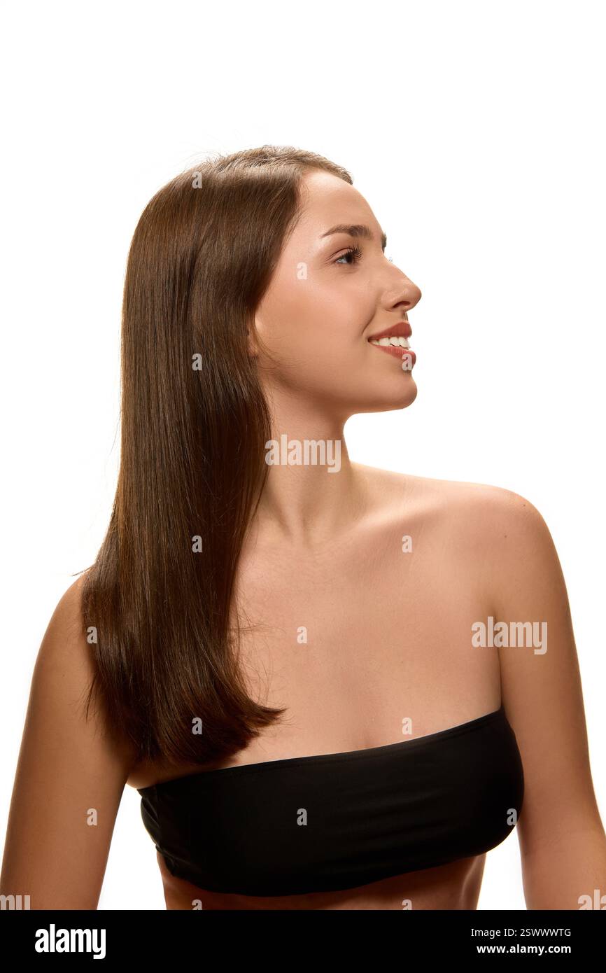 Young attractive woman in black top smiling while looking sideways, shows her shining hair ...