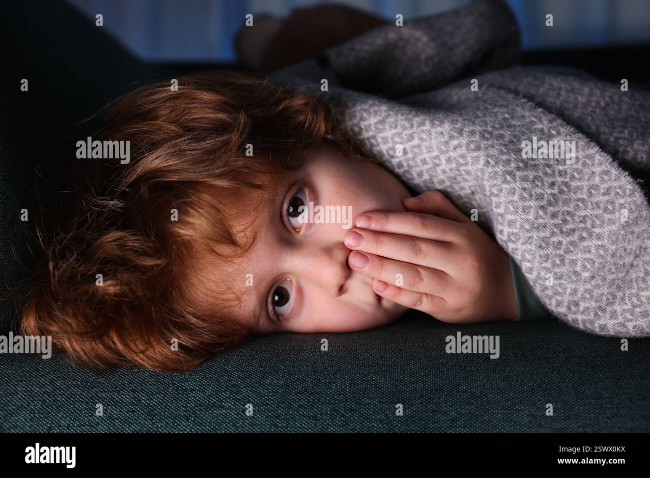 Afraid boy hiding under blanket on sofa at night Stock Photo - Alamy