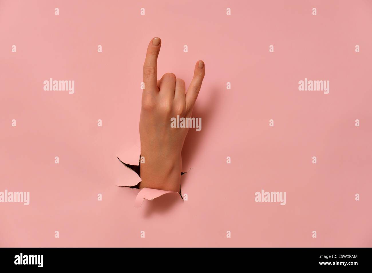 Hand making rock gesture through torn pink paper. Minimal creative ...